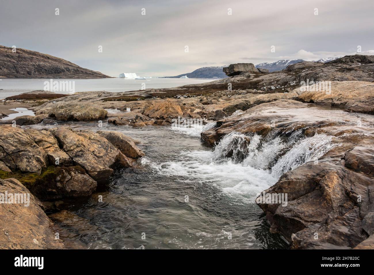 Waterfalls flowing from Milne Land into O Fjord and the large icebergs ...