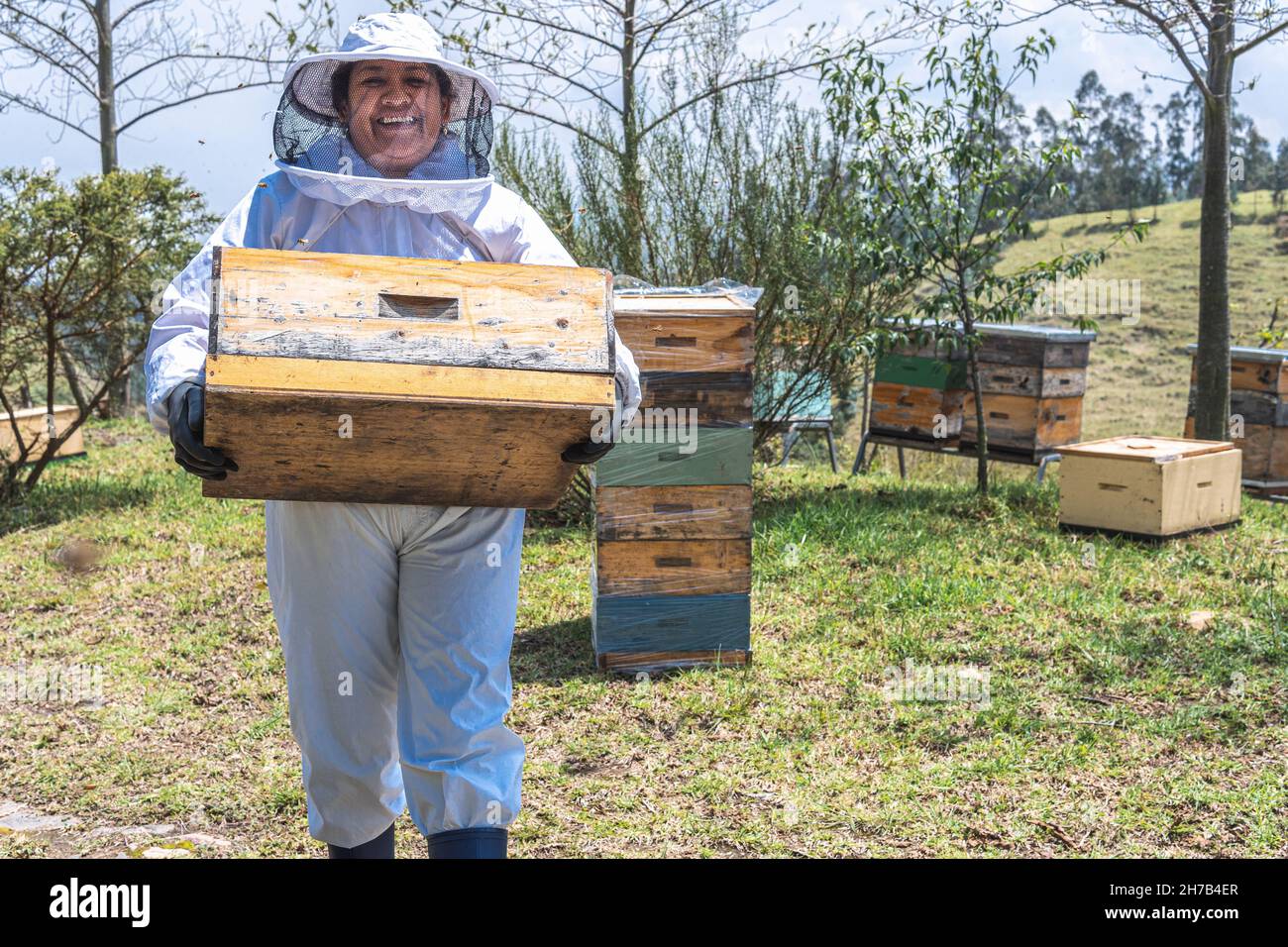 Portrait of a female beekeeper in protective suit carrying a crate of ...