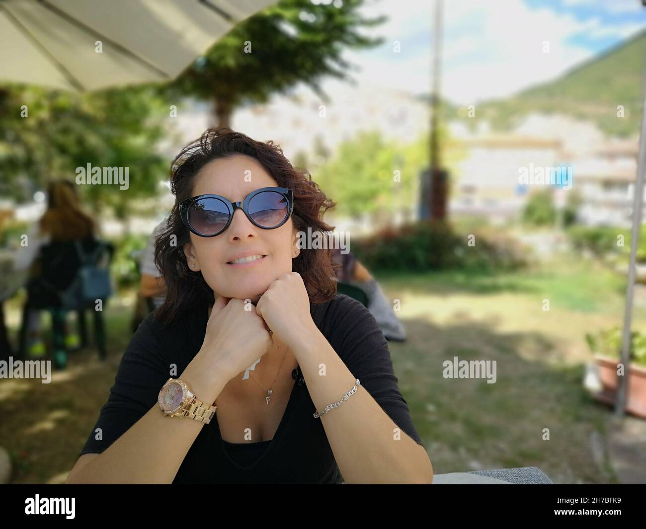 Smiling Italian woman wearing sunglasses with hands under her face ...