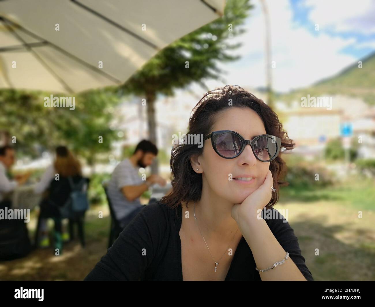 Smiling Italian woman wearing sunglasses with a hand under her face ...