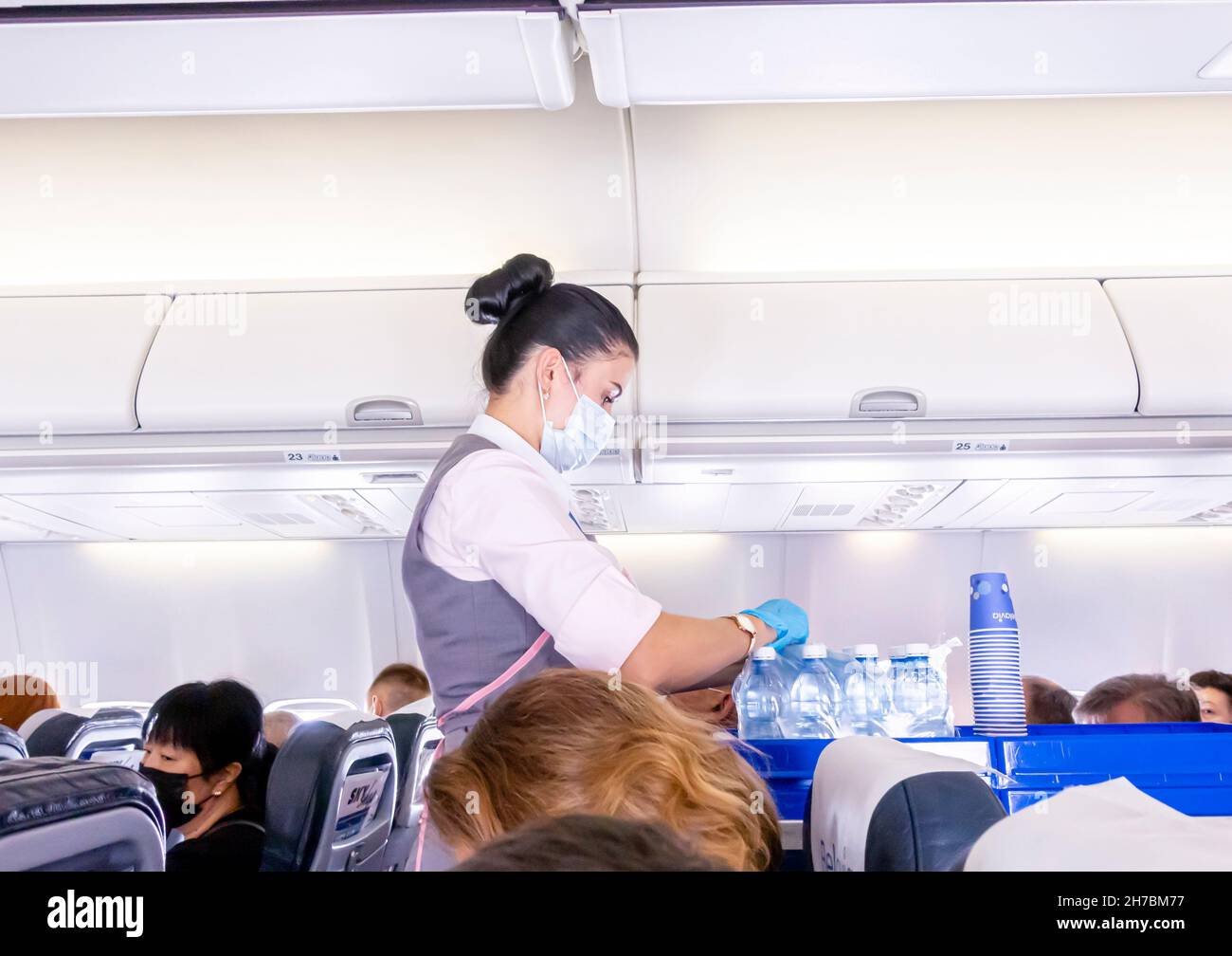 Female flight attendant in face mask serving water drinks to passengers ...