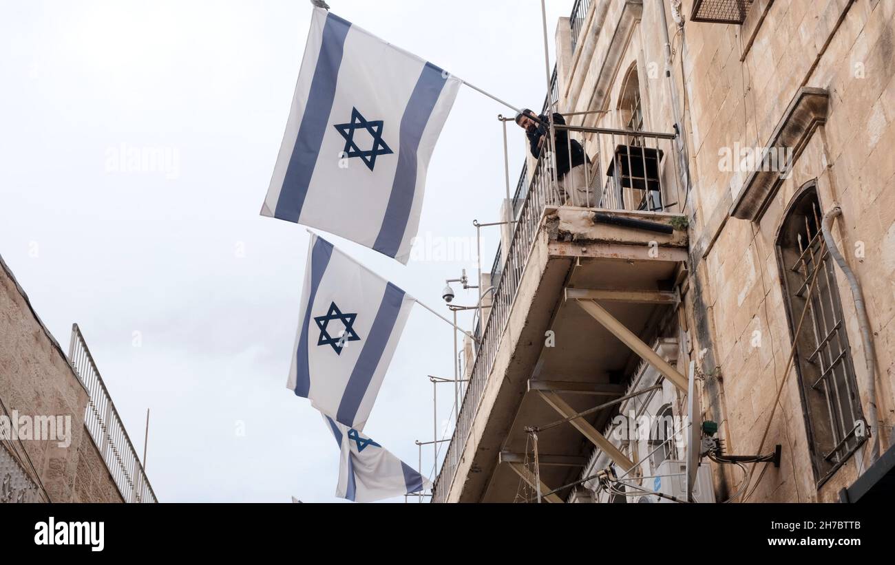 A Jewish settler stands on a balcony adorned with Israeli flags in Al ...