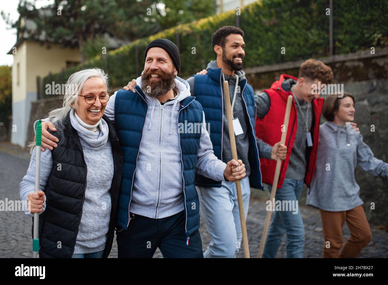 Diverse group of happy volunteers walking with tools to do street clean ...