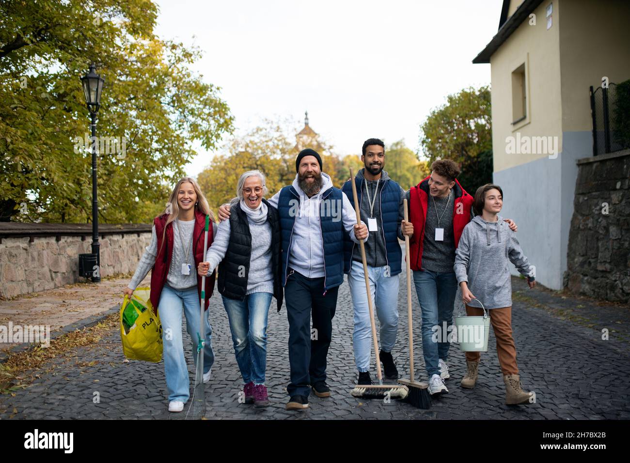 Diverse group of happy volunteers walking with tools to do street clean ...