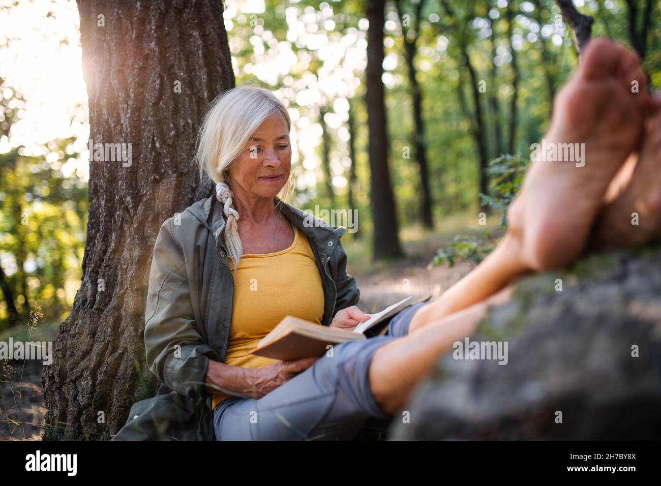 Senior woman relaxing and reading book outdoors in forest Stock Photo ...