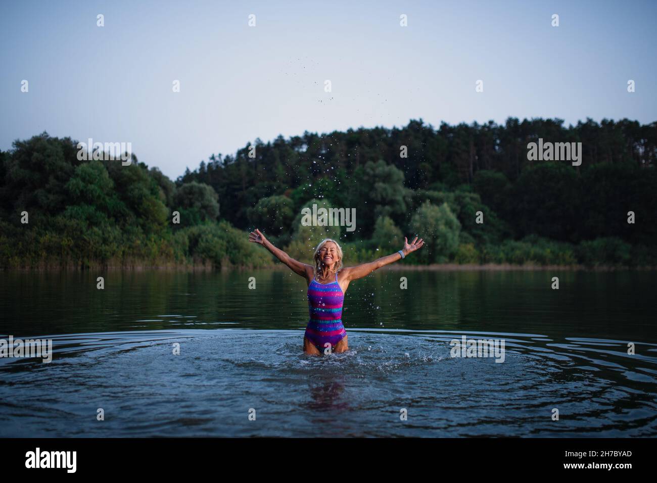 Happy active senior woman swimmer splashing water outdoors in lake ...