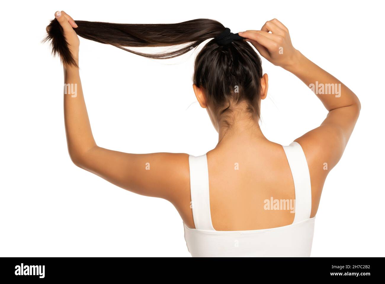 Back view of a young woman adjusting her hair in a ponytail on a white ...