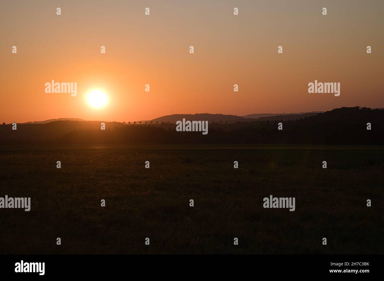 romantic sunset behind a hill in front of a meadow. Tuscan view with ...
