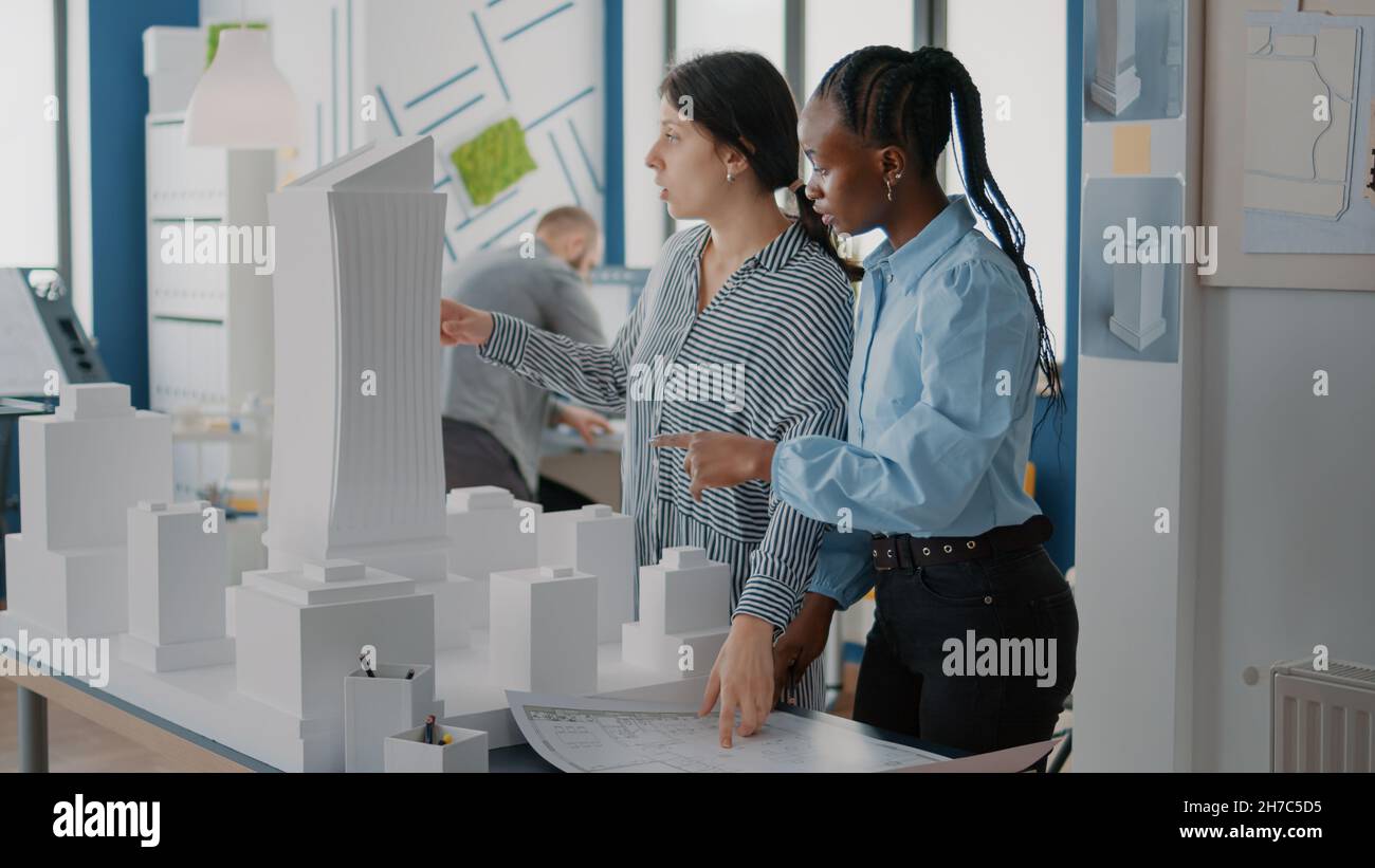 Workmates Analyzing Blueprints Plan And Building Model On Table Working On Construction Women