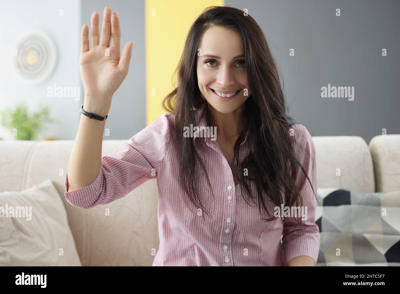 Beautiful young woman lift hand as hello gesture sit in living room ...