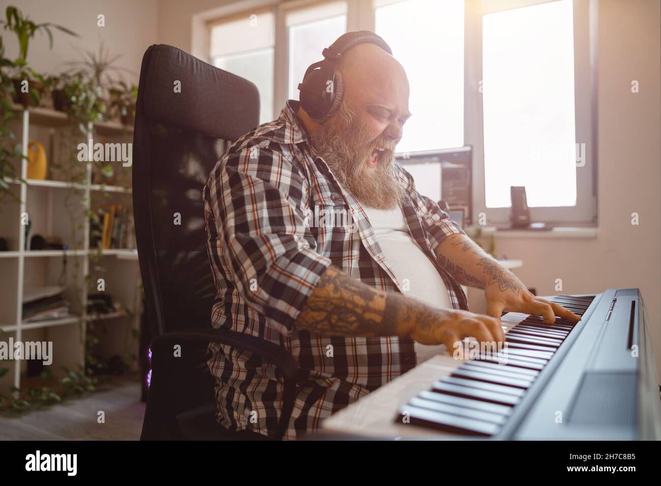 Emotional plump man composer writes music playing sound synthesizer in ...