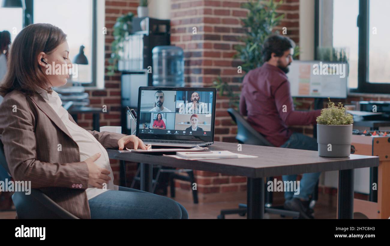 Pregnant woman talking to colleagues on video call, using laptop at ...