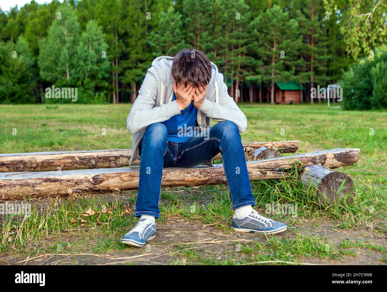 Sad Young Man sit on the Log outdoor Stock Photo - Alamy