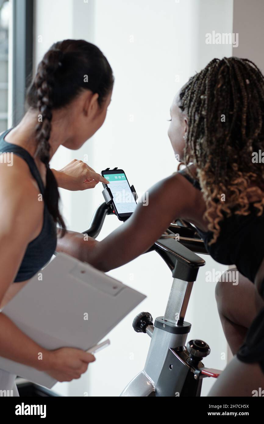 Fitness trainer showing client how to control speed on exercise bike in ...