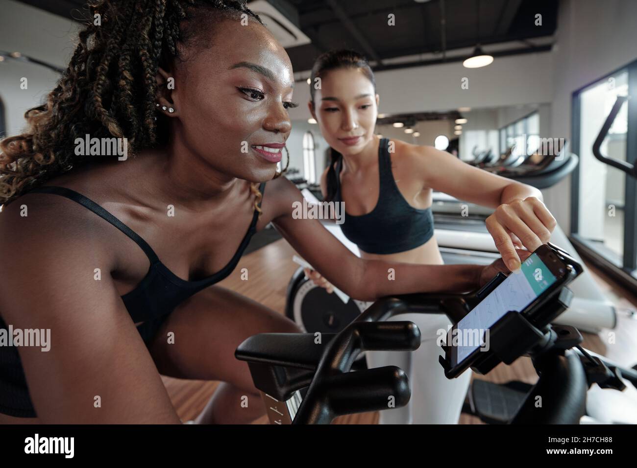Fitness trainer explaining female client how to checking her progress via application on ...
