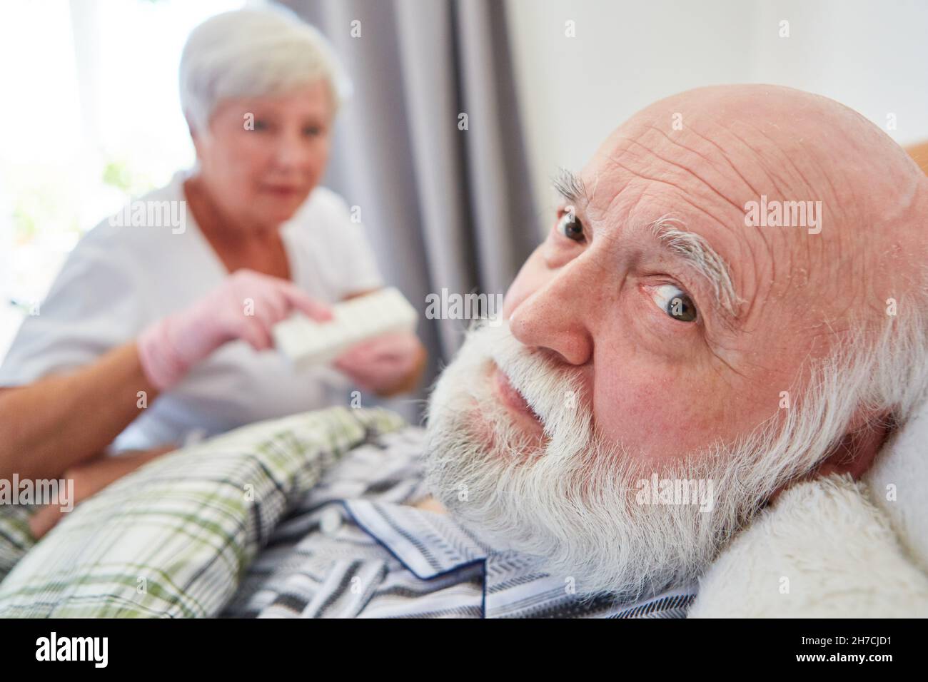 Sick senior in bed in nursing home and geriatric nurse with medication ...