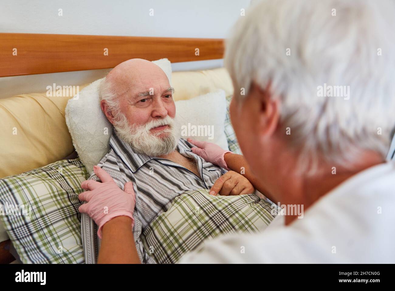 Geriatric nurse comforts old man as patient in bed in nursing home or ...