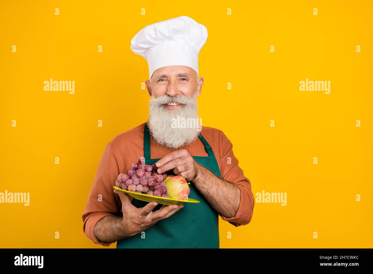 Portrait of attractive cheery grey-haired man chef eating snack fresh ...