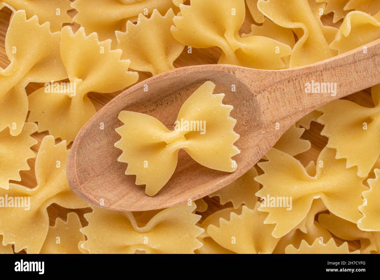 Light yellow butterfly pasta with a wooden spoon, close-up, top view ...