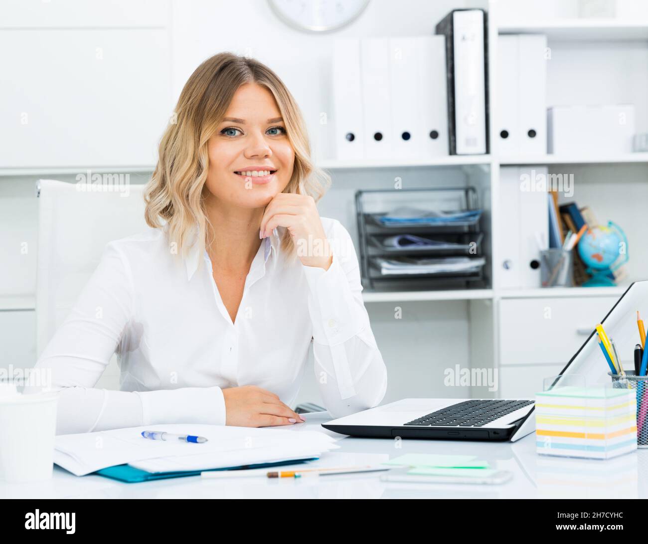 Friendly girl in corporate type clothes sitting at office desk in ...