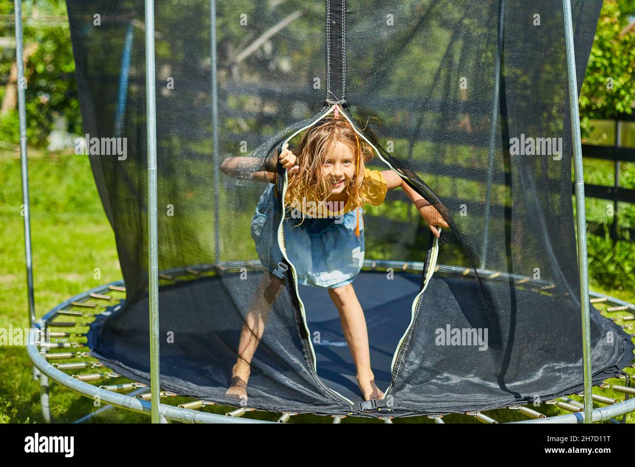 Happy little child jumping on trampoline in the backyard of the house ...