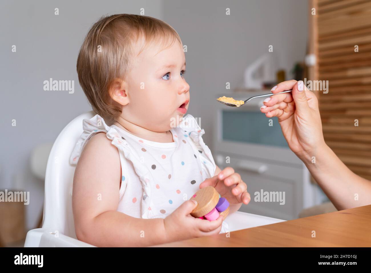 Faceless mother feeding baby. Child on high chair. First solid for ...