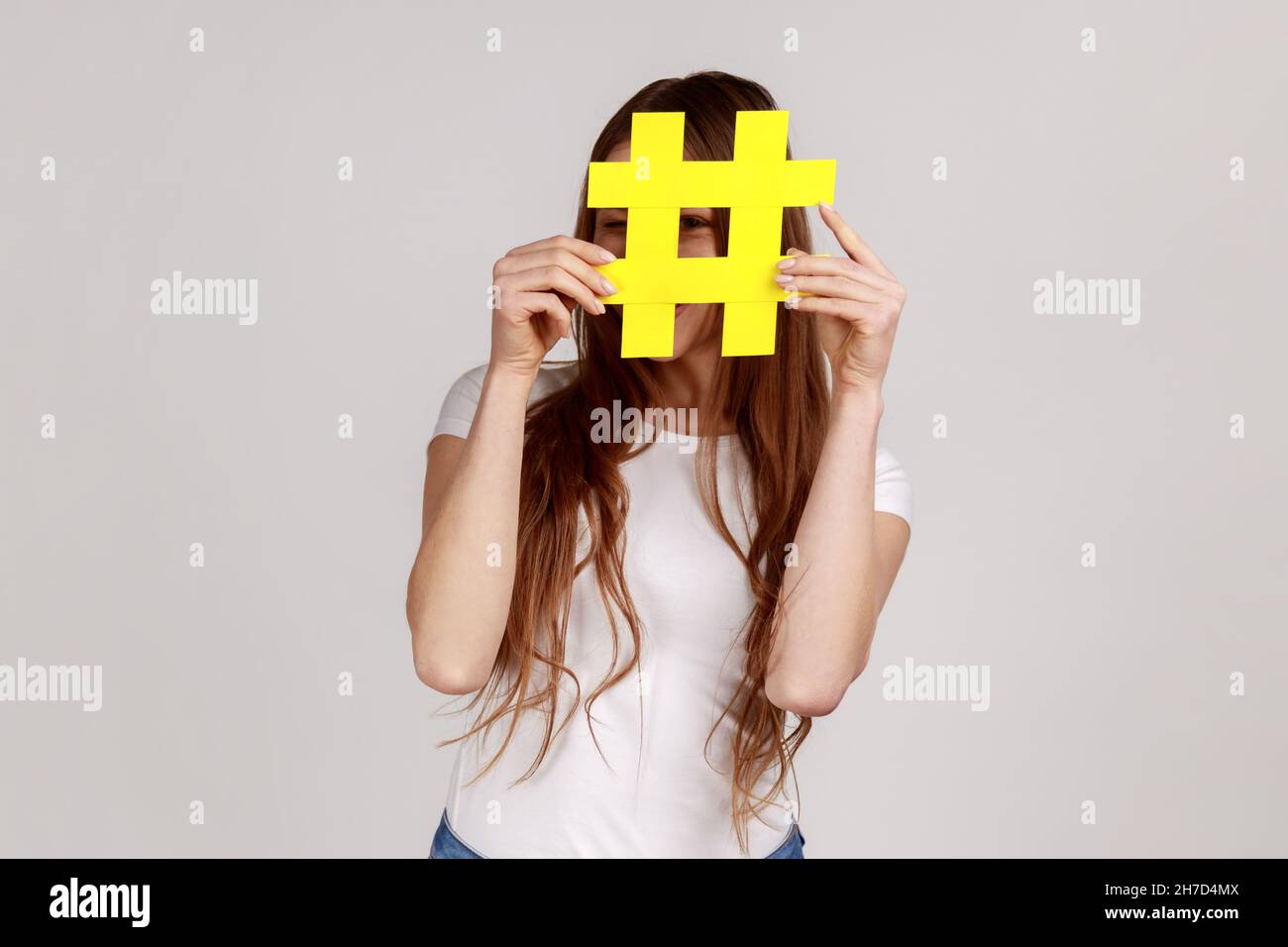 Playful woman hiding behind yellow hashtag symbol, covering face with ...