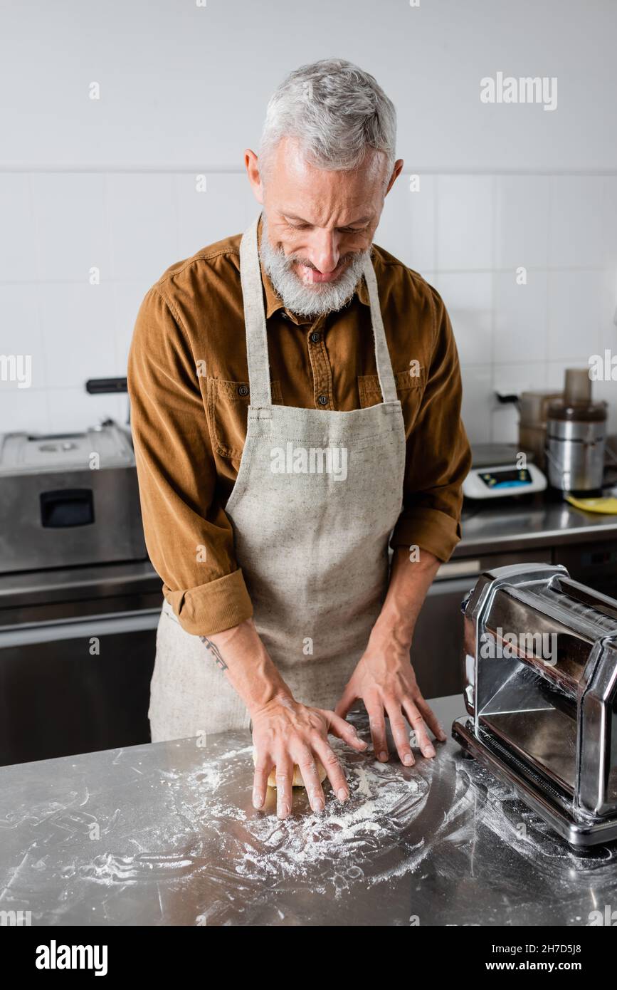 Mature chef making dough near pasta maker machine in kitchen Stock ...
