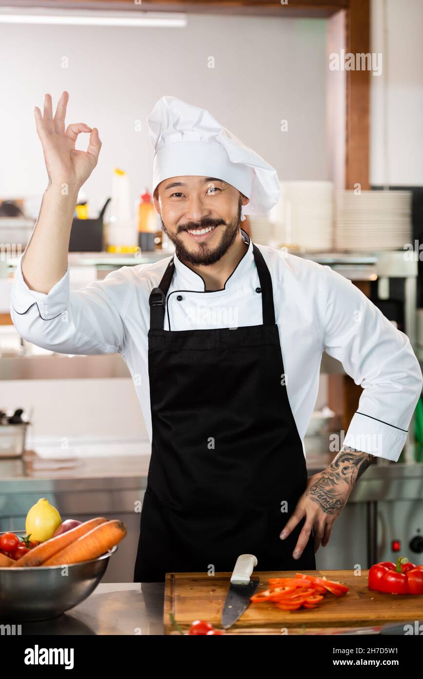 Smiling asian chef showing okay gesture near cutting board and ...