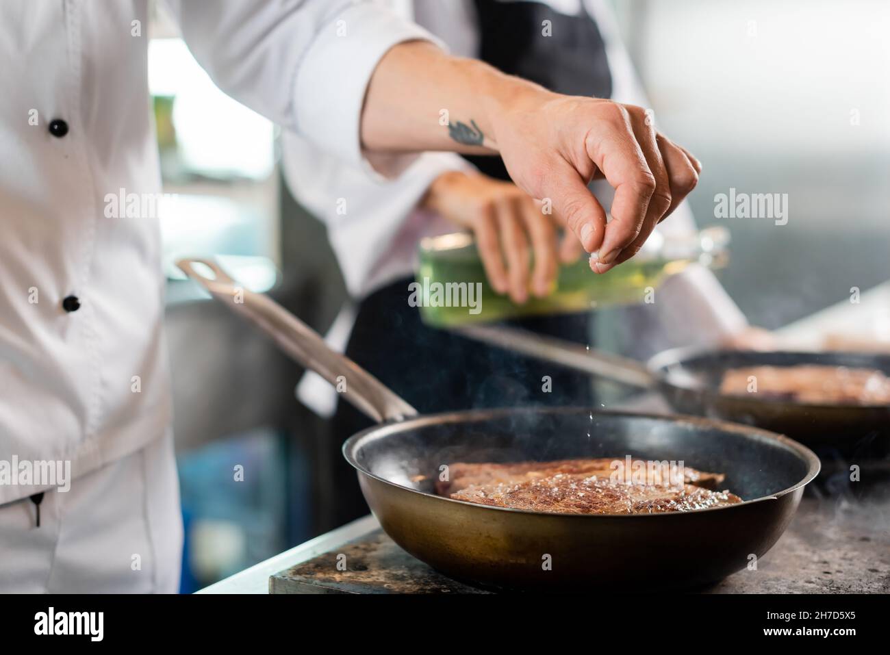 Cropped view of chef pouring salt while cooking meat on frying pan in ...