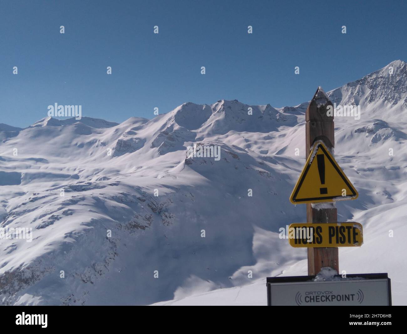 Yellow warning sign on the mountain road with a snowy range in Tignes ...