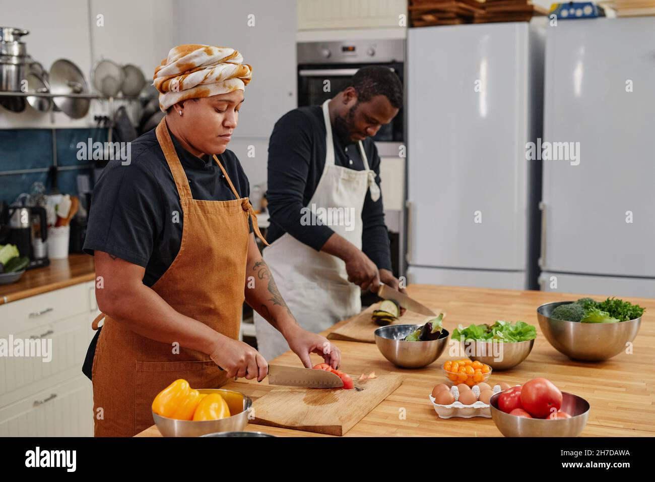 Side view portrait of two people wearing aprons while cooking together ...