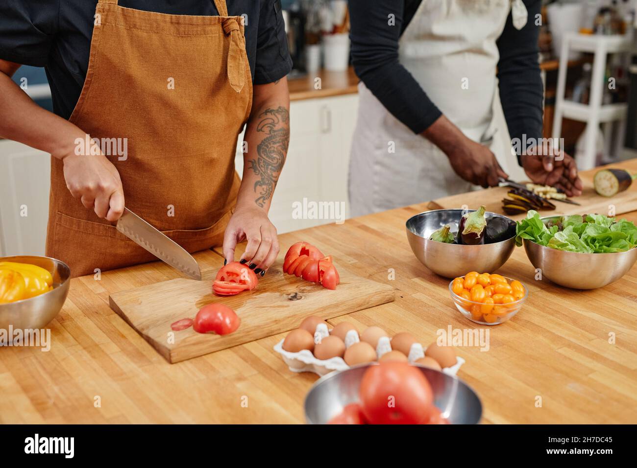 Close up of unrecognizable people cutting vegetables while cooking ...