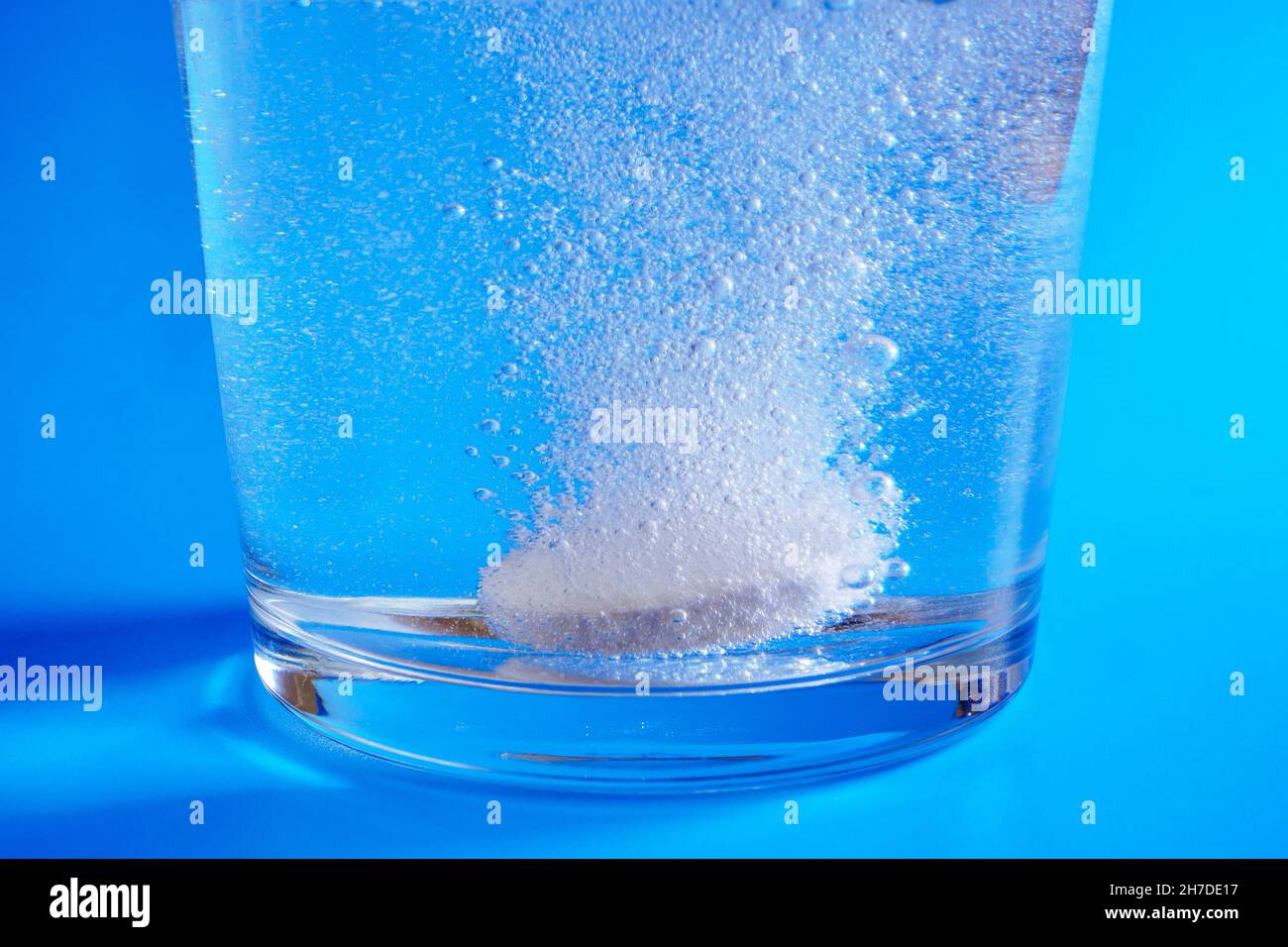 Closeup of effervescent tablet dissolving in glass of water on blue ...
