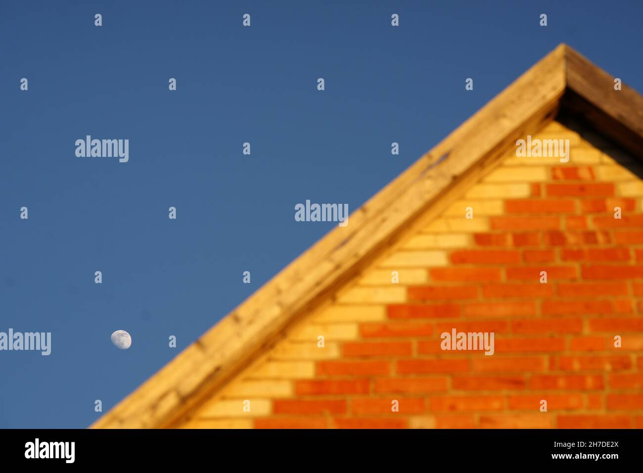 Orange brick house roof and growing moon in clear blue sky during the ...