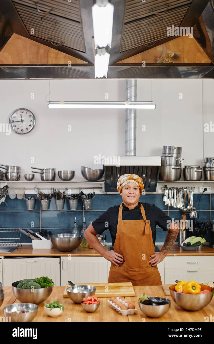 Vertical portrait of smiling female cook looking at camera while posing ...
