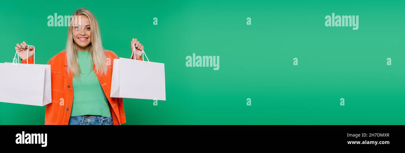 happy blonde woman in trendy clothes looking at camera while showing ...