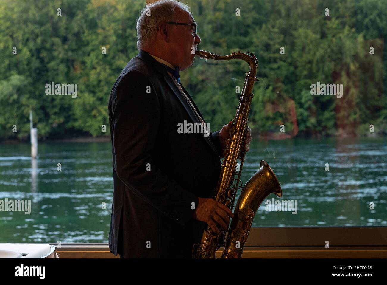 Saxophone player playing jazz in front of windows with forest and blue ...