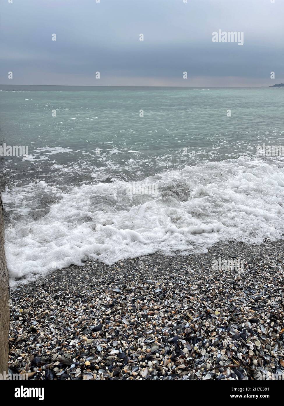 Vertical shot of blue wavy waters of the sea washing over seashell ...