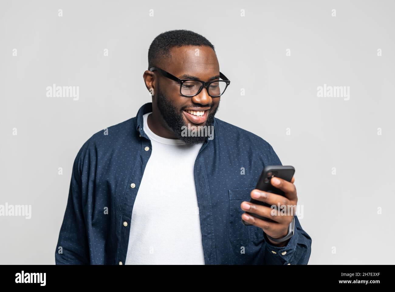 Portrait of cheerful young black guy sending message on mobile phone ...