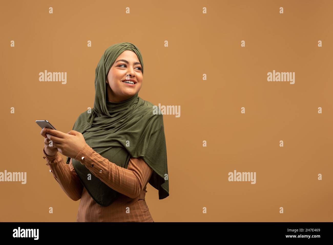 Great ad. Happy muslim woman in headscarf using smartphone and looking ...