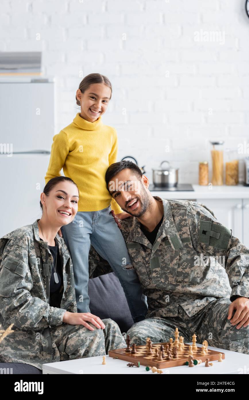 Happy kid standing near parents in military uniform looking at camera ...