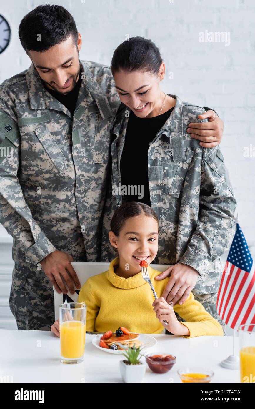 Happy parents in military uniform standing near daughter with breakfast ...