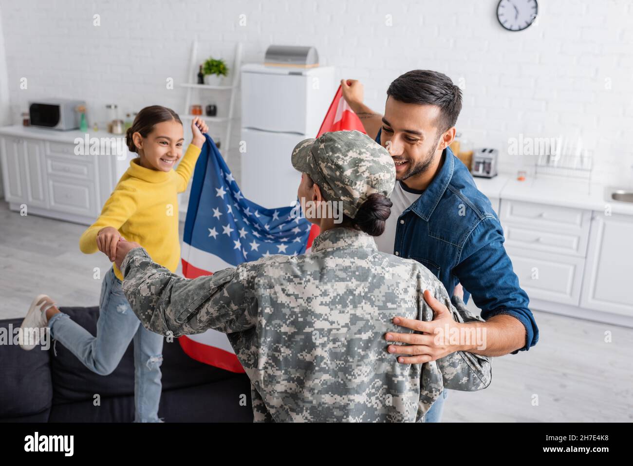 Positive family with american flag hugging woman in military uniform in ...