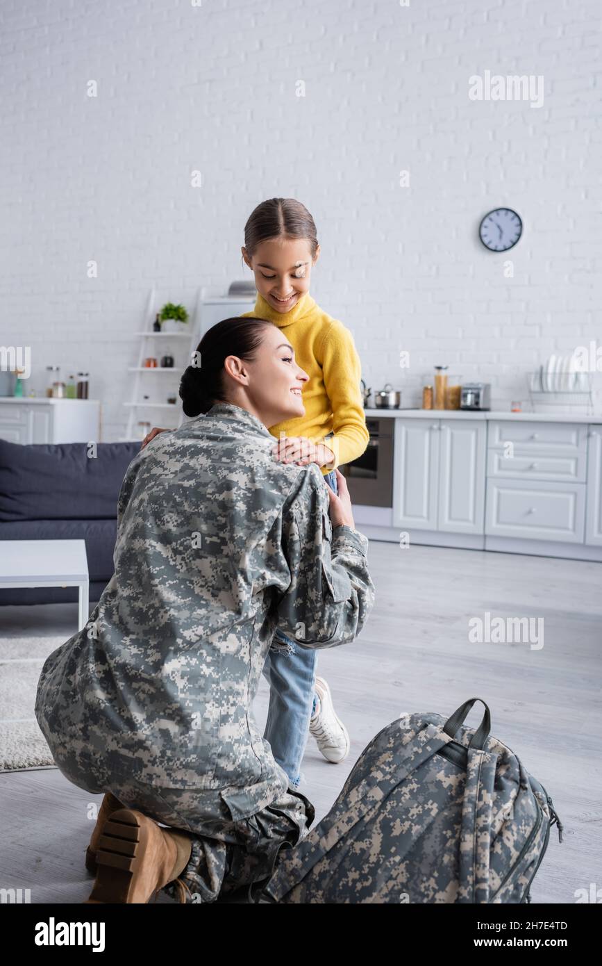Smiling woman hugging child near military backpack at home Stock Photo ...