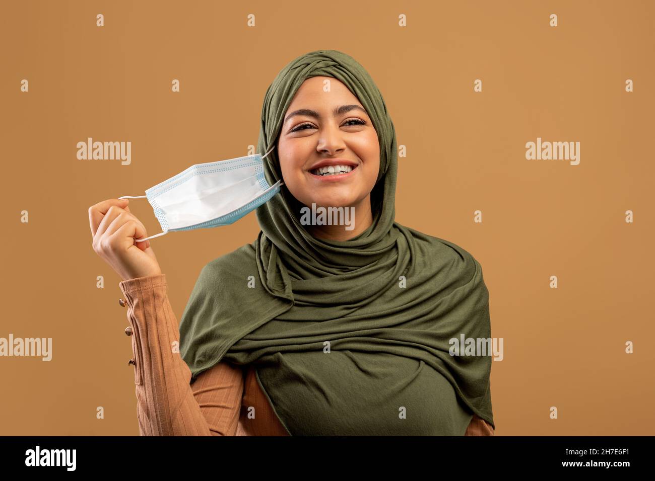 End of the epidemic. Happy arab woman taking off her face mask on brown ...