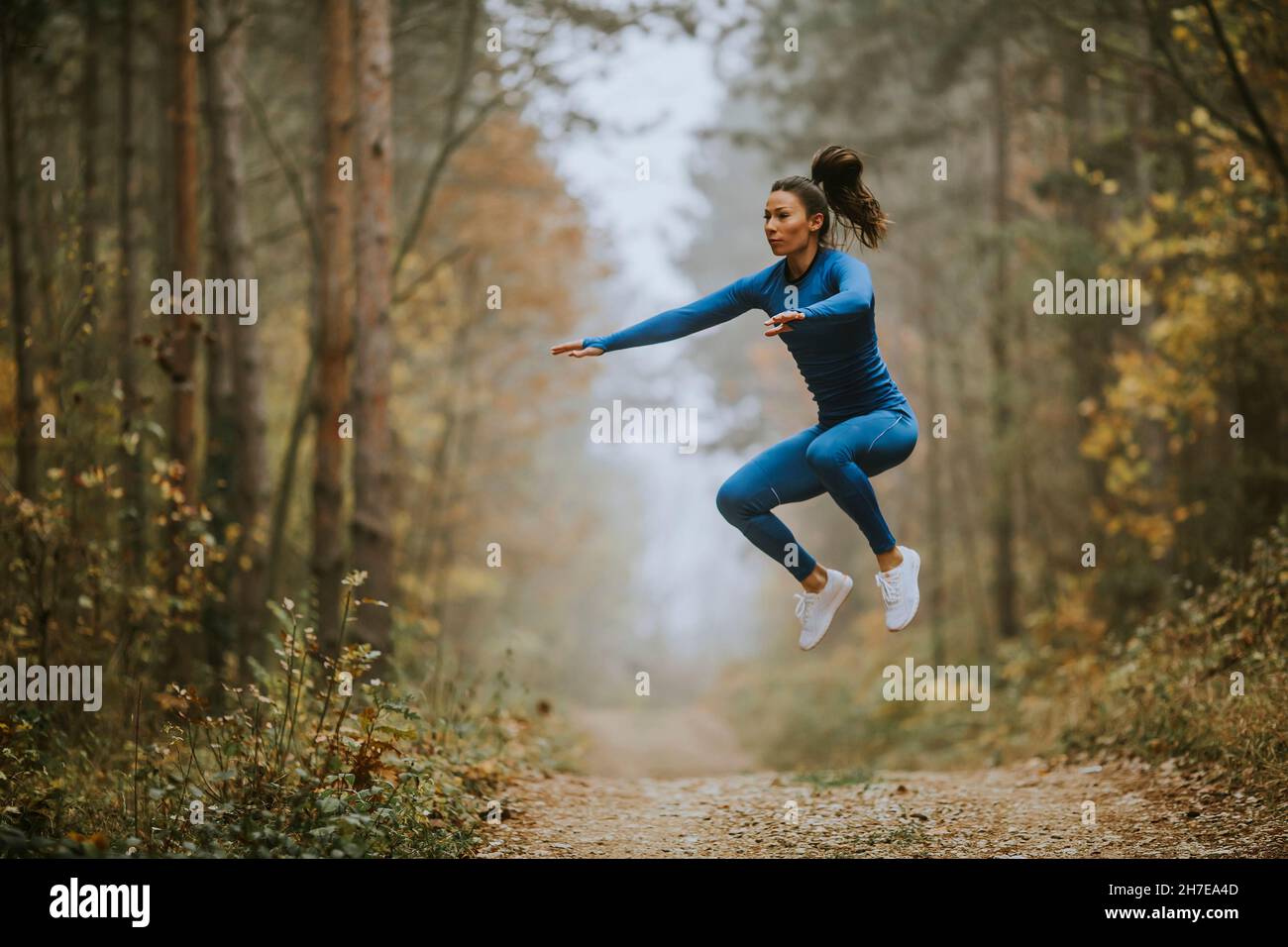 Young woman in blue track suit taking high jump on the forest trail at ...