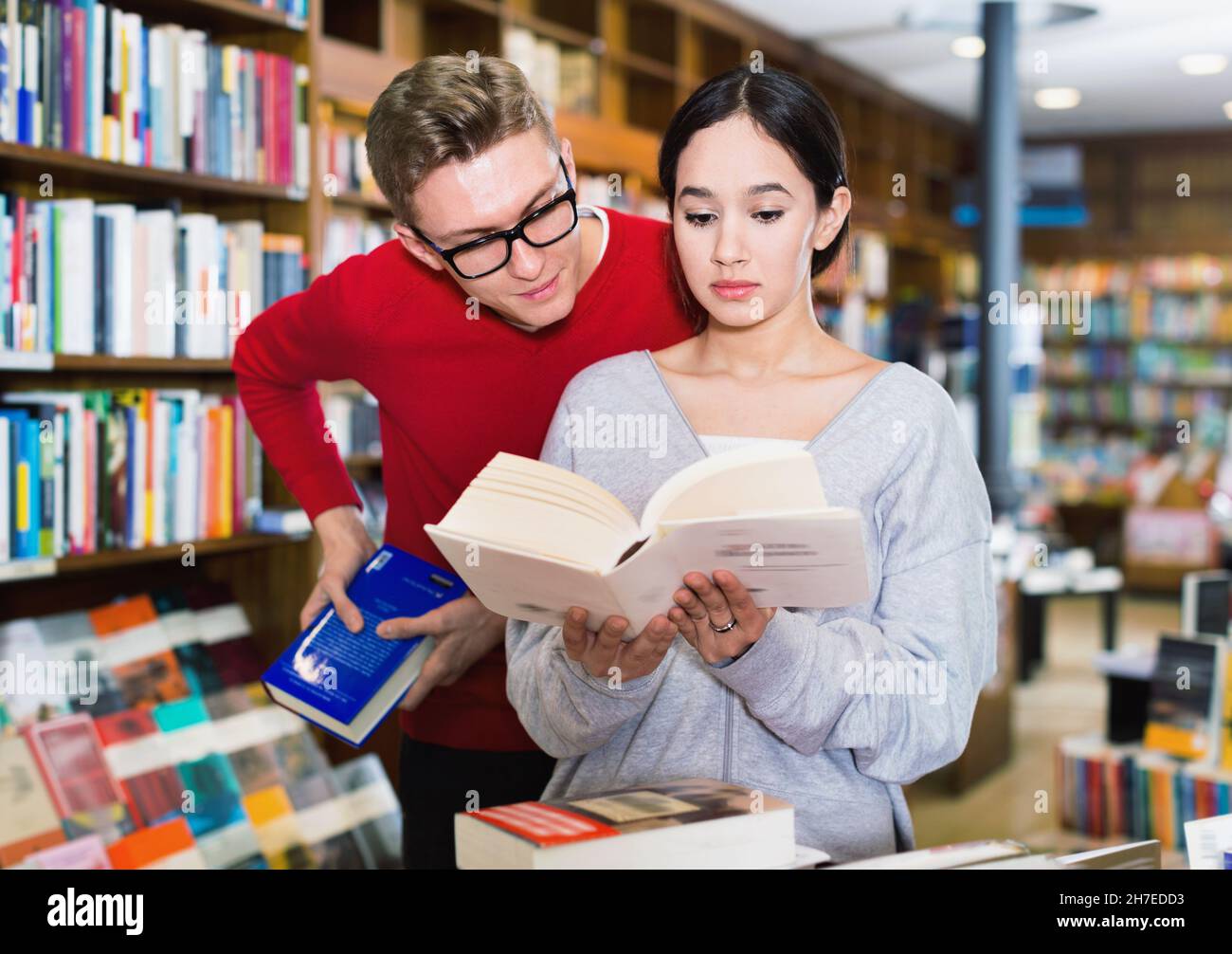 Girl reading book in bookstore while guy looking at her book over her ...