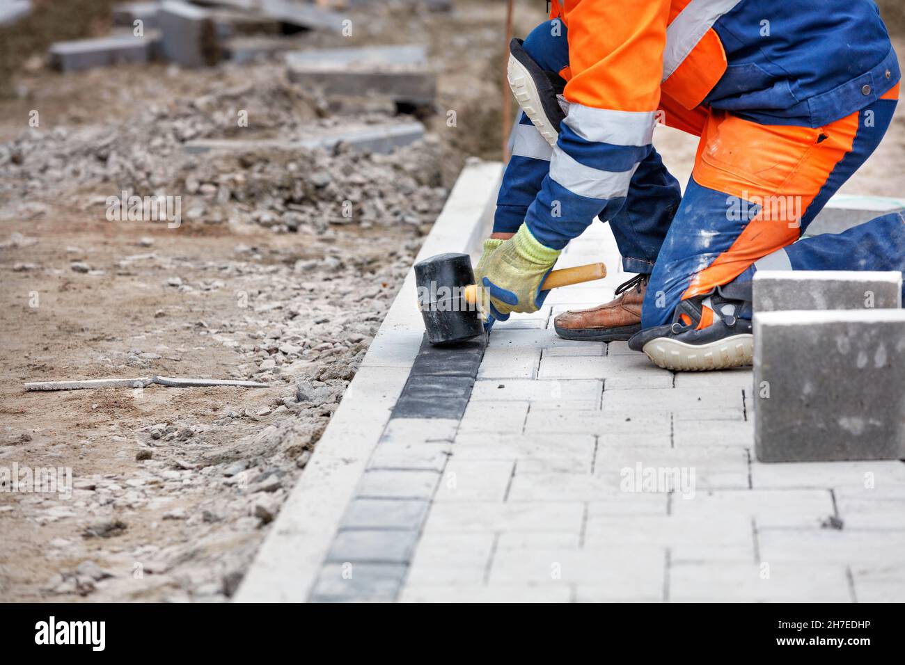 A worker in a blue and orange overalls squatting down and paving slabs ...
