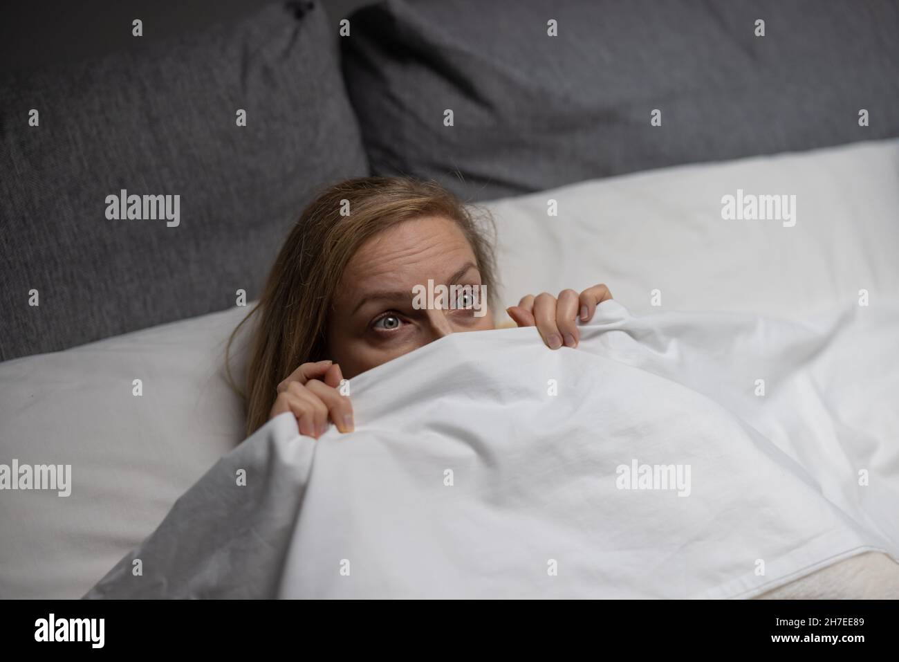 Scared woman lying in bed Stock Photo - Alamy
